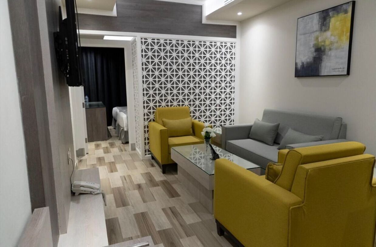 Uma sala de estar moderna com um sofá, poltronas amarelas, uma mesa de centro e uma televisão.