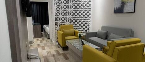 Uma sala de estar moderna com um sofá, poltronas amarelas, uma mesa de centro e uma televisão.