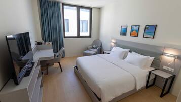 Quarto de hotel com cama, escrivaninha, cadeira, televisão e janela com cortinas.