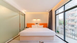 Quarto de hotel moderno com uma cama grande, uma mesinha de cabeceira e vista para a cidade através de amplas janelas.
