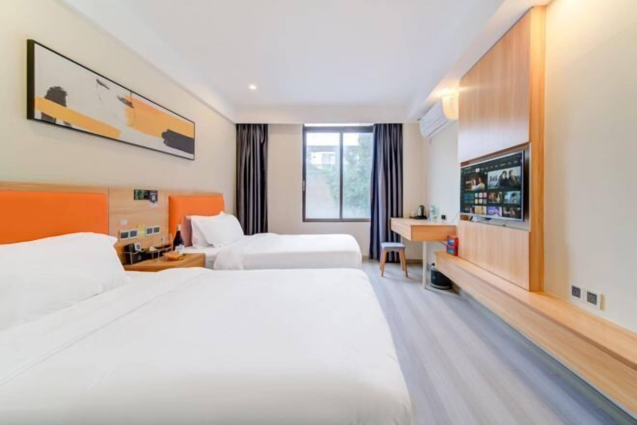 Quarto de hotel com duas camas, uma escrivaninha, televisão e janela com cortinas.