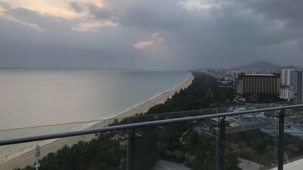 Paisagem costeira com praia, edifícios e uma montanha ao longe.