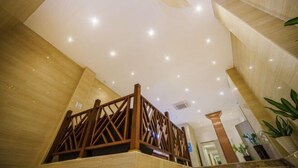 Um interior moderno com escada de madeira, luzes embutidas no teto e um lustre decorativo.