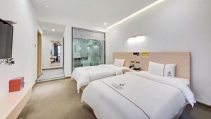 Quarto de hotel com duas camas, uma televisão, uma escrivaninha e uma porta de vidro para o banheiro.