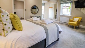 Quarto de hotel com cama, cadeira, televisão e janela com cortinas.