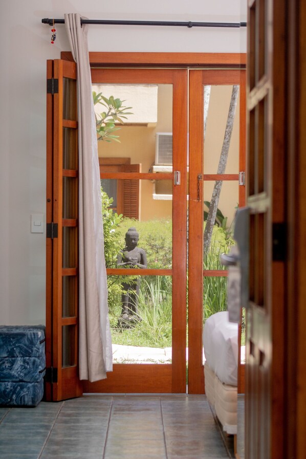 Quarto com cama, sofá azul e porta de madeira que dá para uma varanda com estátua e plantas.