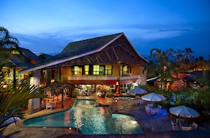 Um resort com uma piscina grande, área de estar ao ar livre e um edifício bem iluminado.