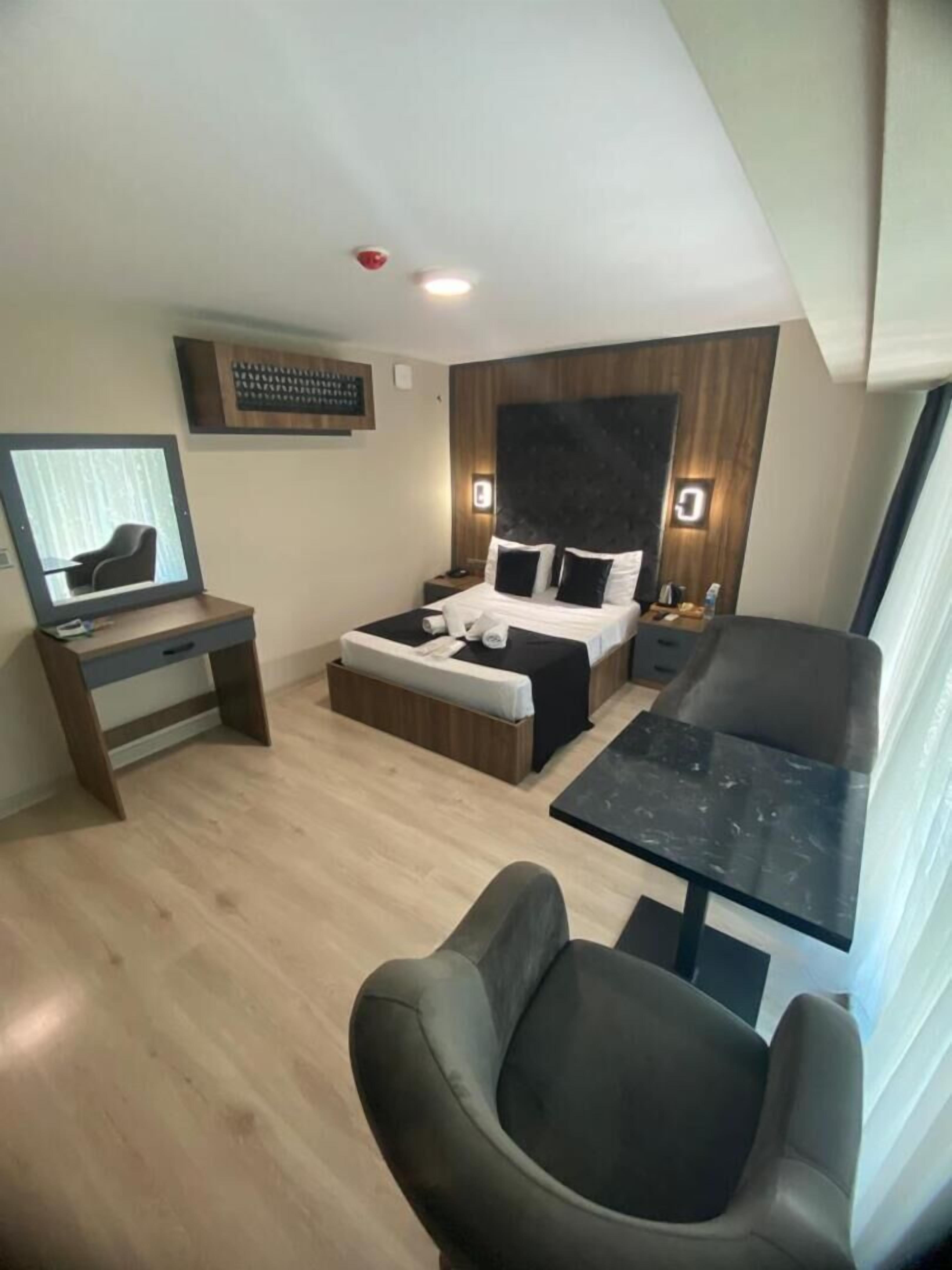 Quarto de hotel compacto, com cama, escrivaninha, cadeira e mesa pequena.