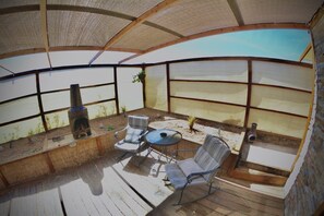 Um alpendre coberto com mesa e cadeiras, uma lareira e vista para o exterior.