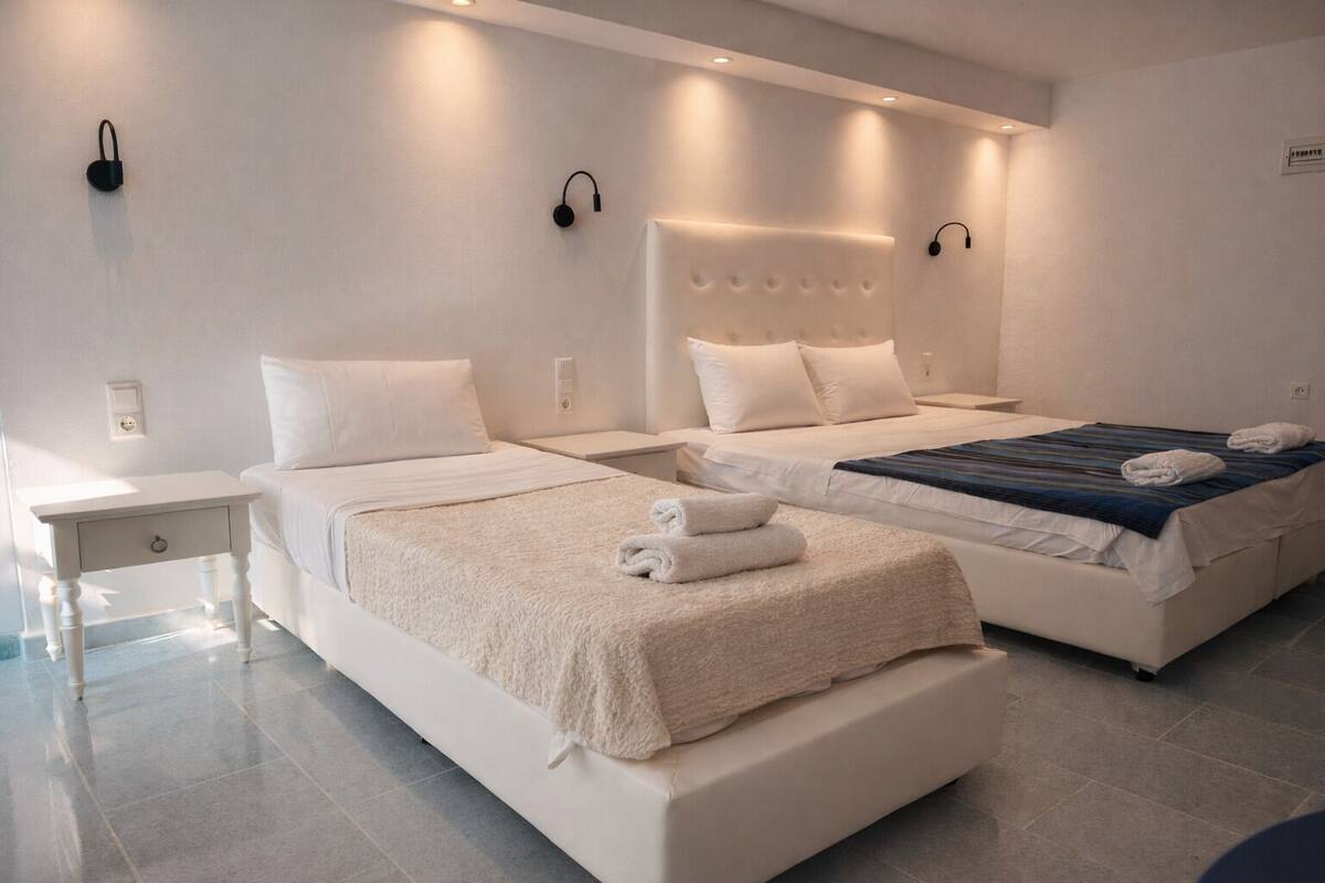 Quarto de hotel moderno com duas camas, mesa de cabeceira e iluminação embutida na parede.