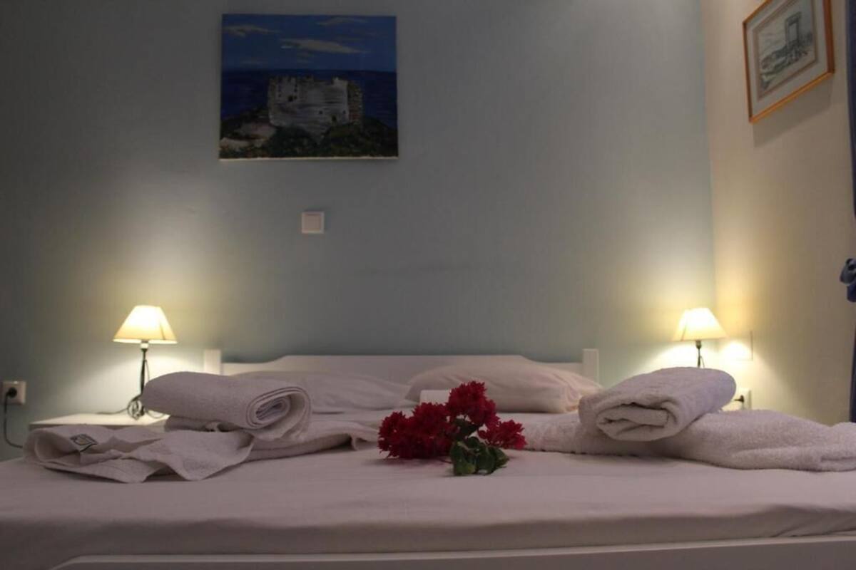 Quarto de hotel com cama, duas luminárias de cabeceira, um quadro na parede e um buquê de flores.