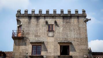 Um edifício de pedra com ameias, duas janelas e uma pequena varanda.