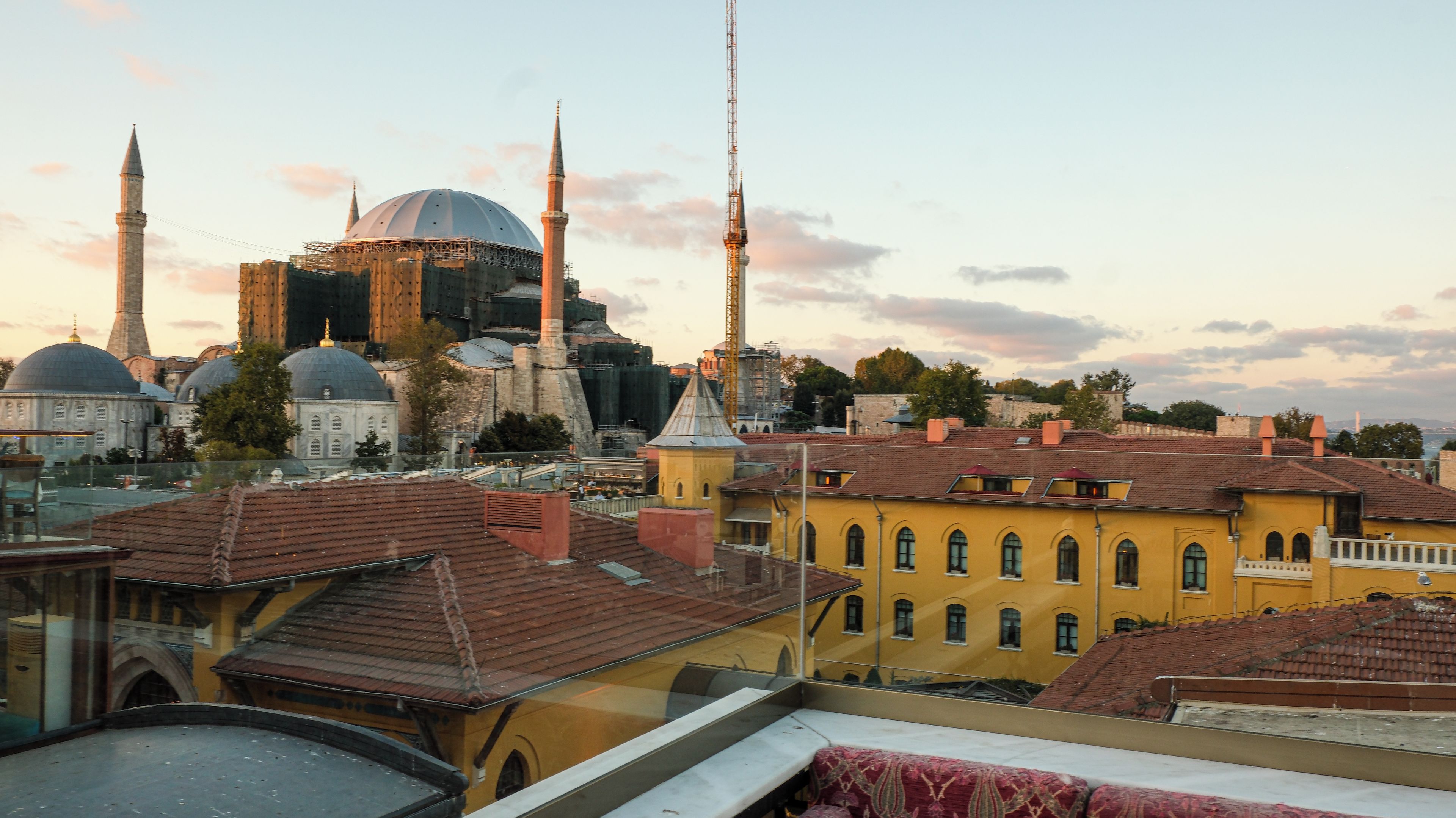 Vista de um horizonte urbano com edifícios históricos, incluindo uma mesquita com uma grande cúpula e minaretes, e um edifício amarelo com telhado vermelho.