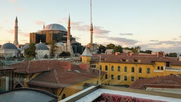 Vista de um horizonte urbano com edifícios históricos, incluindo uma mesquita com uma grande cúpula e minaretes, e um edifício amarelo com telhado vermelho.
