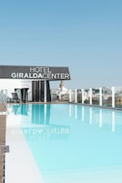 Uma área de piscina de hotel com uma placa indicando 'HOTEL GIRALDACENTER' e um horizonte urbano ao fundo.