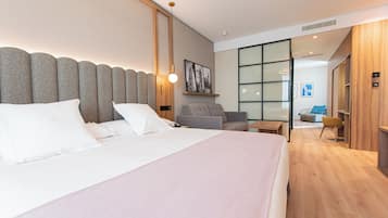 Quarto de hotel moderno com uma cama grande, área de estar com uma cadeira e uma mesinha, e uma janela ampla.