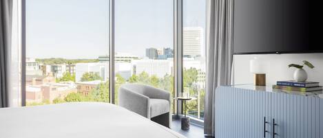 Quarto de hotel com uma cama grande, uma cadeira, uma televisão e vista para a cidade.