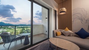 Varanda com vista para a paisagem urbana e montanhas, sofá com almofadas e luminária suspensa.