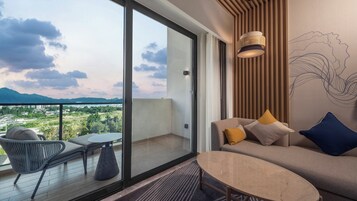 Varanda com vista para a paisagem urbana e montanhas, sofá com almofadas e luminária suspensa.