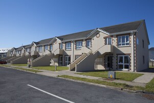 Uma fileira de casas geminadas modernas, com dois andares e estilo arquitetônico uniforme, apresentando uma entrada central com escadas e um gramado bem cuidado na frente.