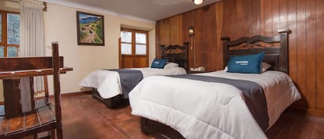 Quarto com duas camas, paredes de madeira, um quadro na parede e uma janela com cortinas.