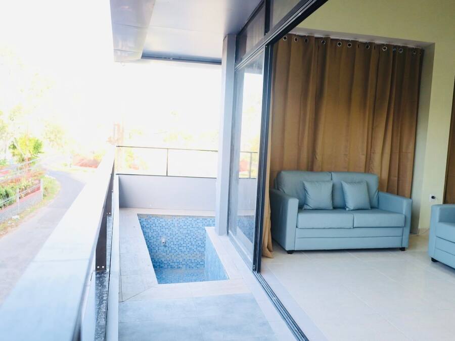 Sala de estar moderna com sofá azul, piscina pequena e vista para a estrada e vegetação lá fora.