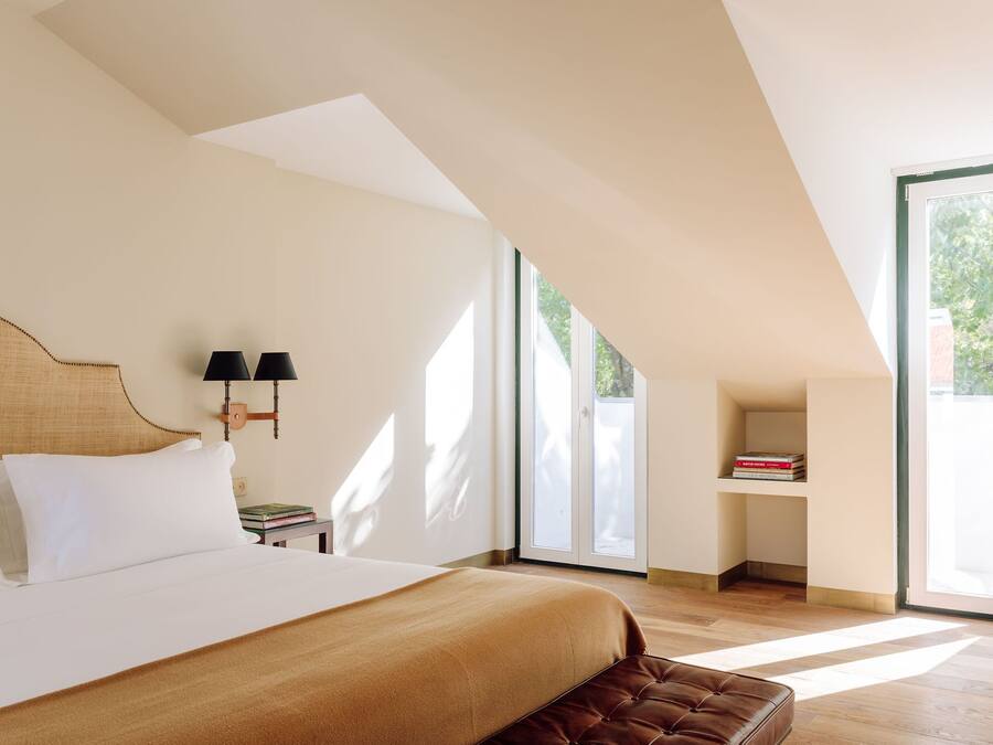 Quarto com cama grande, mesa de cabeceira, abajur e estante embutida com livros.