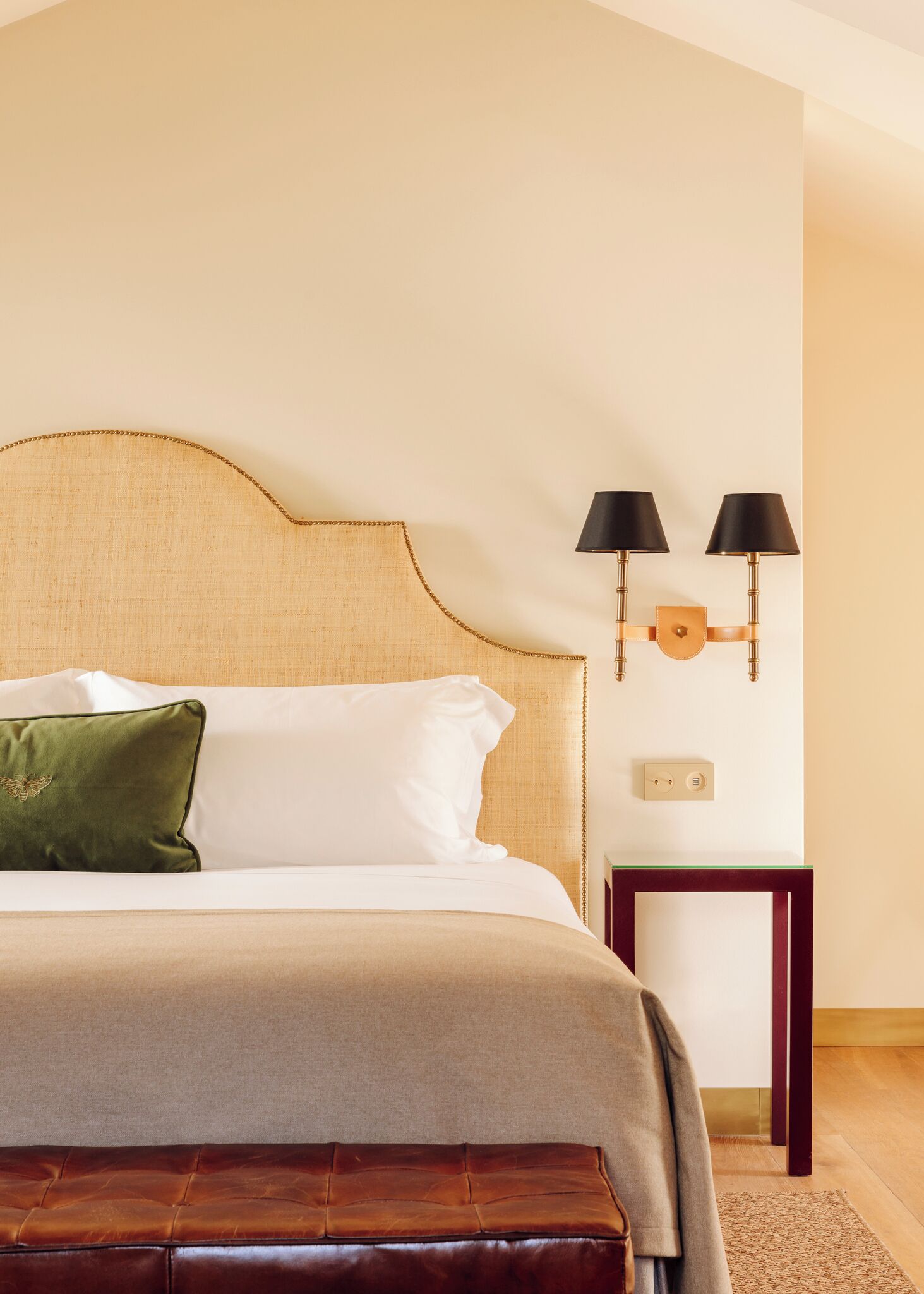 Cama bem arrumada com almofadas brancas e verdes, cabeceira de madeira e duas luminárias fixadas na parede.