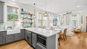 Uma cozinha moderna com armários cinza, bancada de mármore e um espaço de refeições com mobiliário branco.