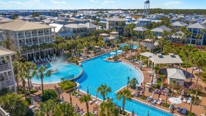 Um resort com várias piscinas, palmeiras e um tanque de água ao fundo.