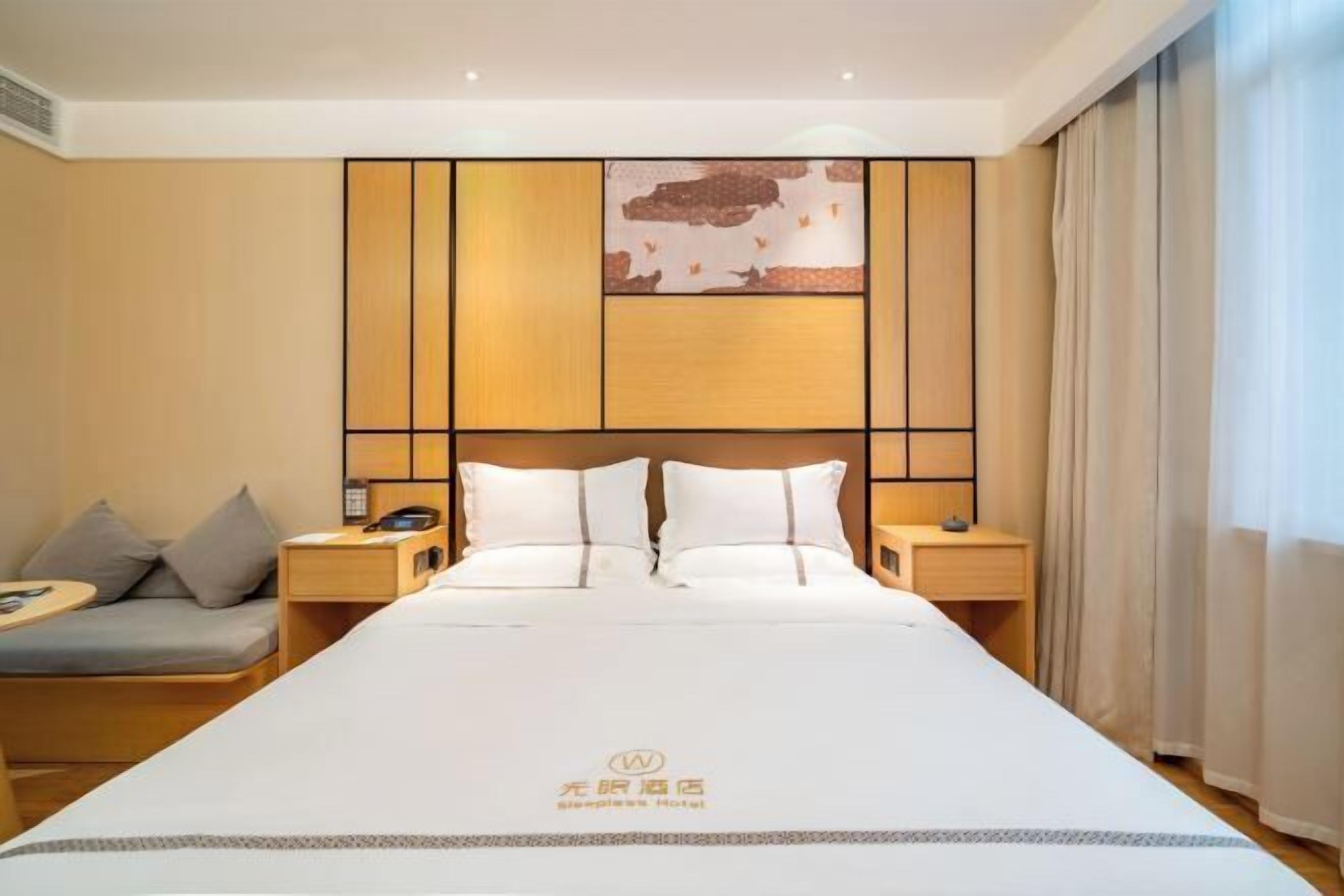 Quarto de hotel com cama grande, duas mesas de cabeceira, um criado-mudo, um sofá e uma parede com painel decorativo.