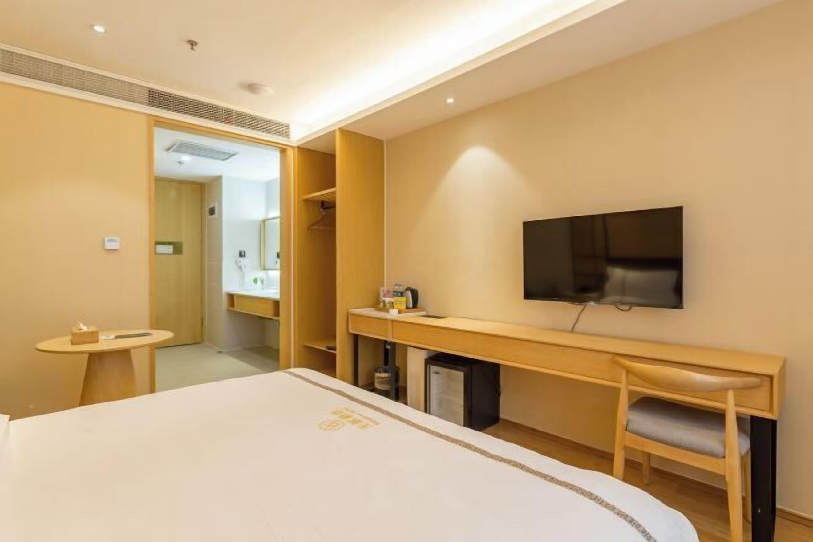 Quarto de hotel com cama, escrivaninha, televisão, espelho e pequena mesa.