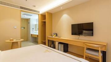 Quarto de hotel com cama, escrivaninha, televisão, espelho e pequena mesa.