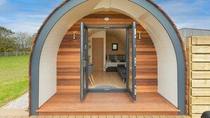 Estrutura de madeira moderna com arco e porta de vidro que dá acesso a um quarto com cama, mesa de cabeceira e um pequeno espaço de estar.