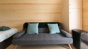 Quarto com sofá cinza, duas almofadas estampadas, manta verde escura e um alto-falante preto.