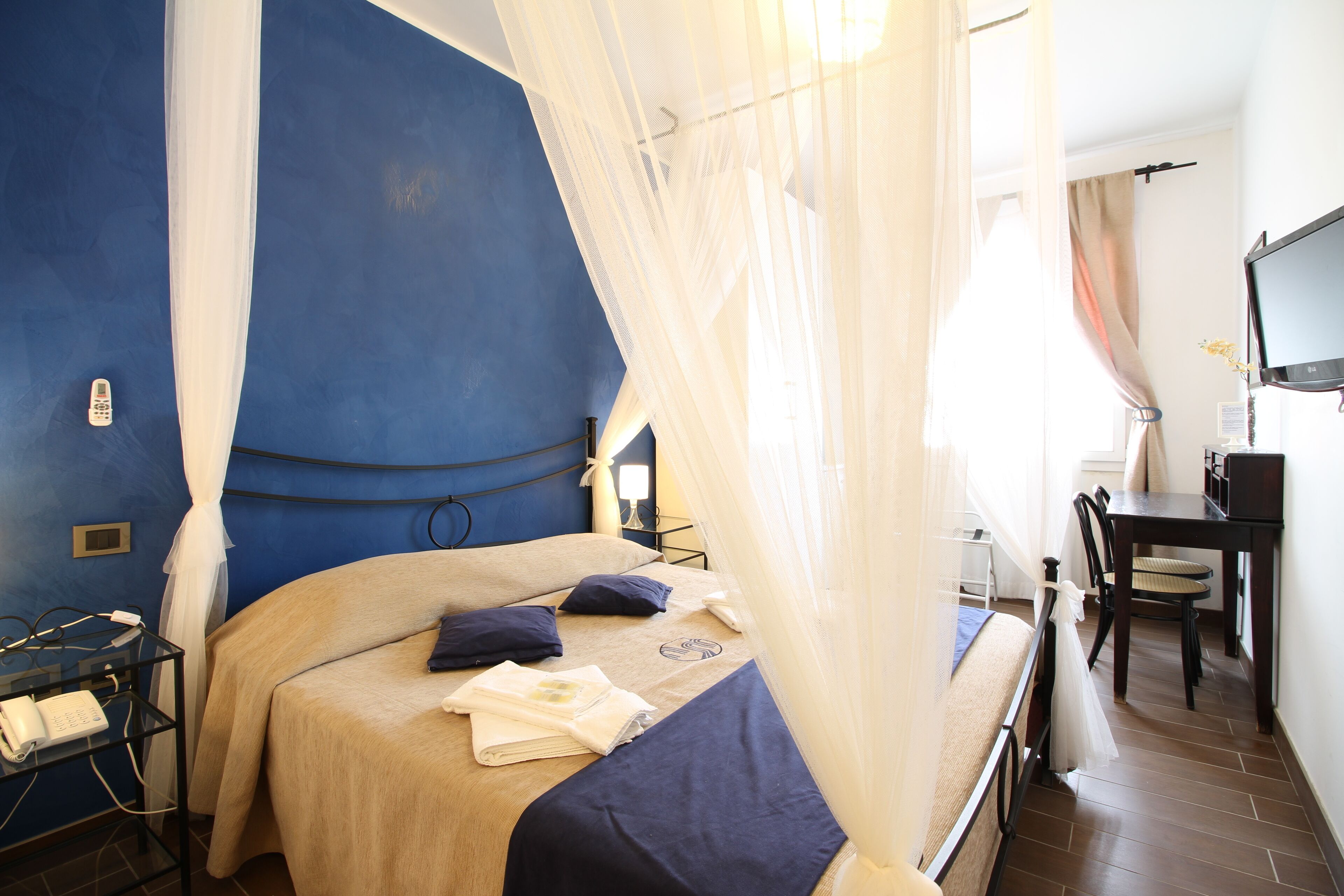 Quarto com cama, escrivaninha, cadeira e televisão.