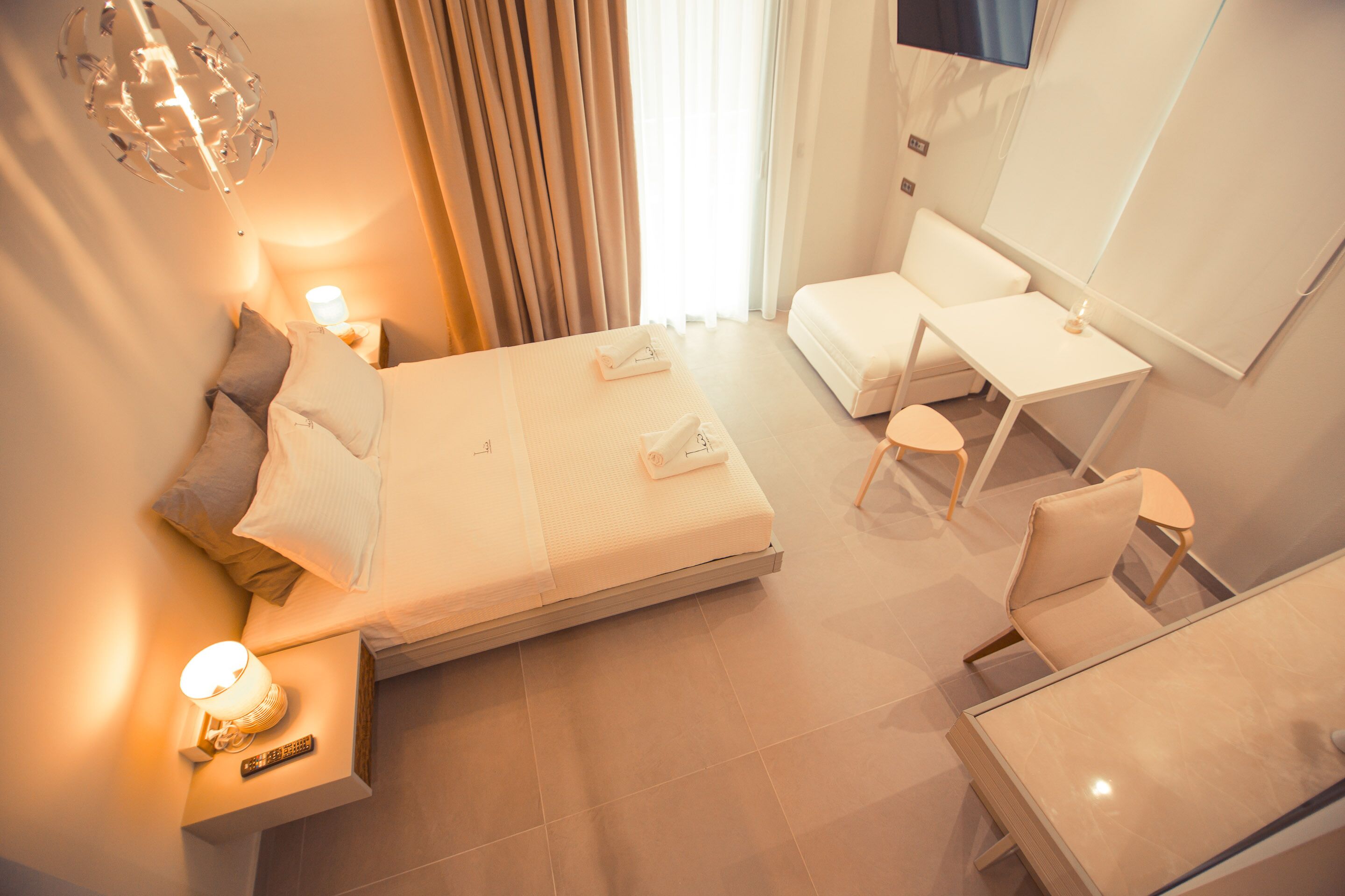 Quarto de hotel com cama, mesa de cabeceira, abajur e uma pequena escrivaninha com cadeira.