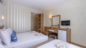 Quarto de hotel com duas camas, uma secretária de madeira com espelho, televisão e um pequeno frigorífico.
