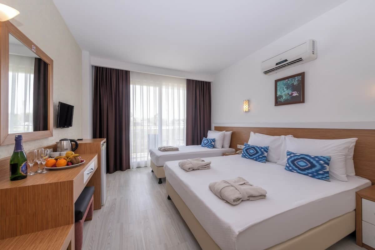 Quarto de hotel com duas camas, uma escrivaninha com espelho, máquina de café e janela com cortinas.
