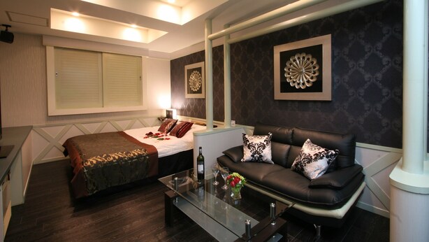 Quarto de hotel moderno com uma cama grande, um sofá de couro, uma mesa de centro de vidro e arte decorativa na parede.