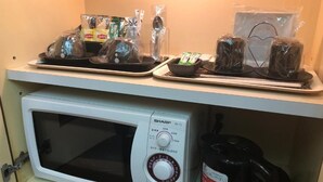 Uma cozinha com micro-ondas, cafeteira e diversos alimentos embalados na bancada.