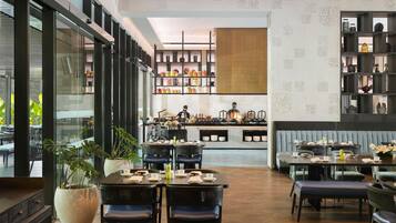 Um restaurante moderno com cozinha central, área de refeições com mesas e cadeiras, e padrões decorativos nas paredes.