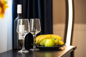 Uma garrafa de vinho, duas taças e um prato com bananas e maçãs sobre uma mesa de madeira.