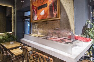 Uma área de buffet com balcão de mármore, estações de serviço bem definidas e um espaço de refeições com mesas e cadeiras de madeira.