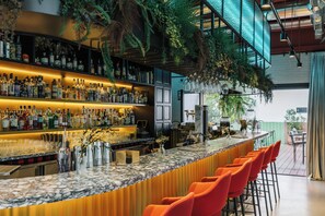 Uma área de bar com bancada de mármore, várias prateleiras cheias de garrafas de bebidas e banquetas laranja.