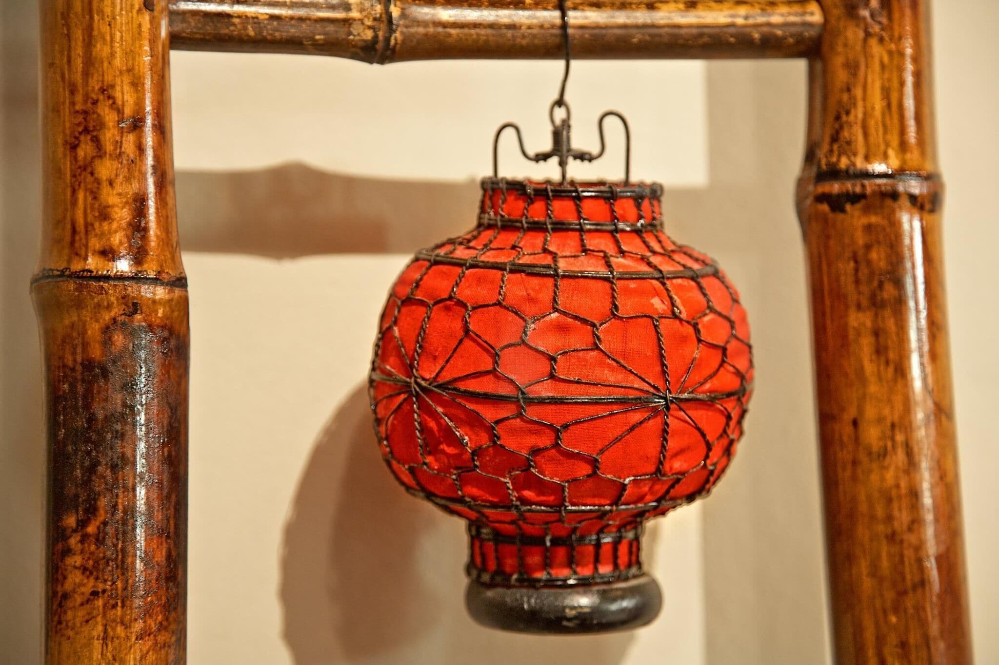 Um vaso de cerâmica vermelha com design de estrutura metálica, pendurado numa estrutura de madeira.