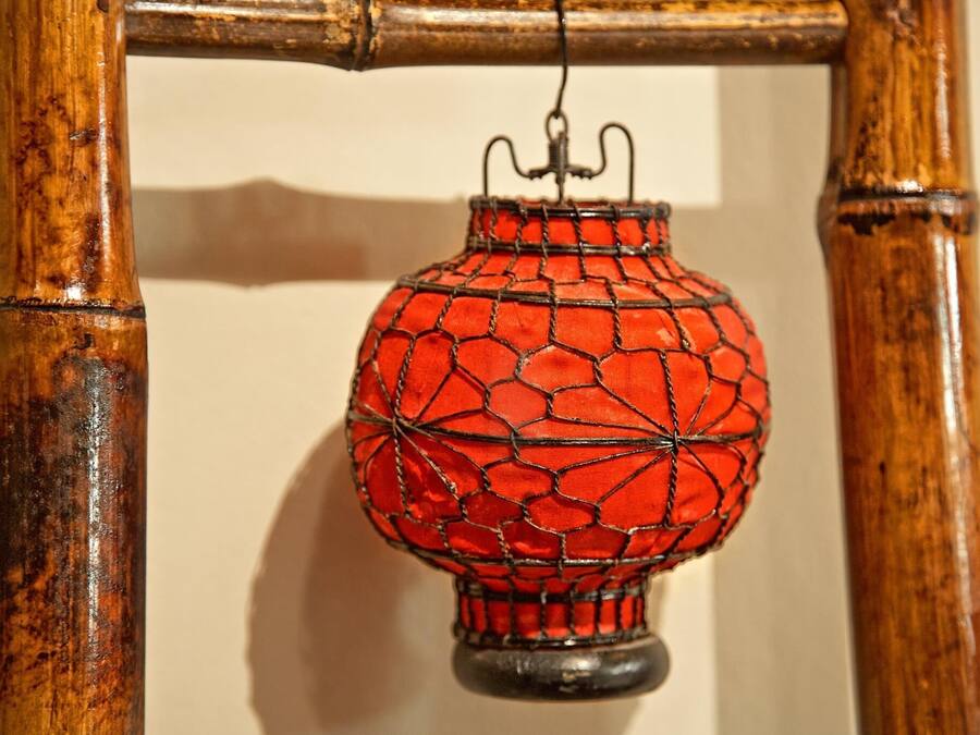 Um vaso de cerâmica vermelha com design de estrutura metálica, pendurado numa estrutura de madeira.