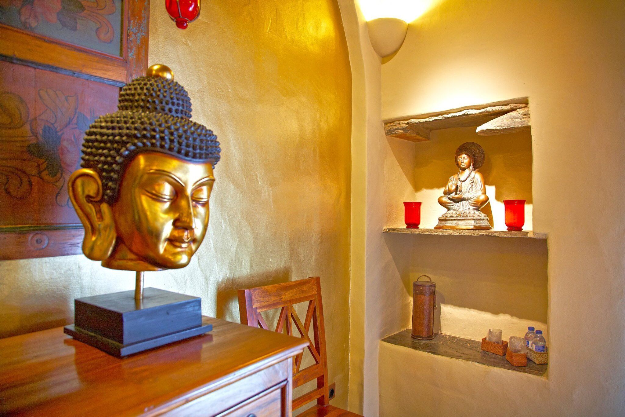 Uma estátua de Buda em uma prateleira, uma cadeira de madeira e uma mesa com uma escultura da cabeça de Buda.