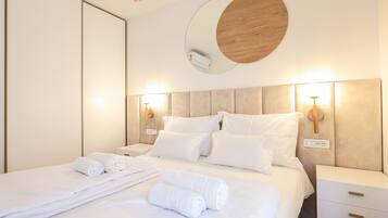 Quarto de hotel moderno com uma cama bem arrumada, duas mesas de cabeceira e um espelho redondo grande na parede.