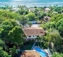 Uma casa grande com piscina, cercada por vegetação exuberante e vista para o oceano.